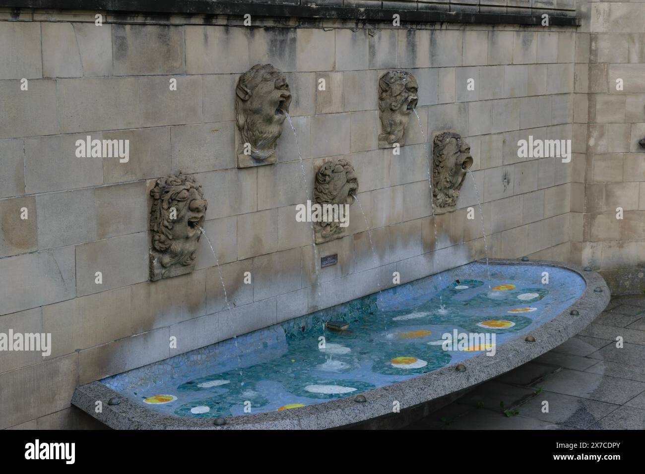 A stone wall with four lion head sculptures spouting water into a ...