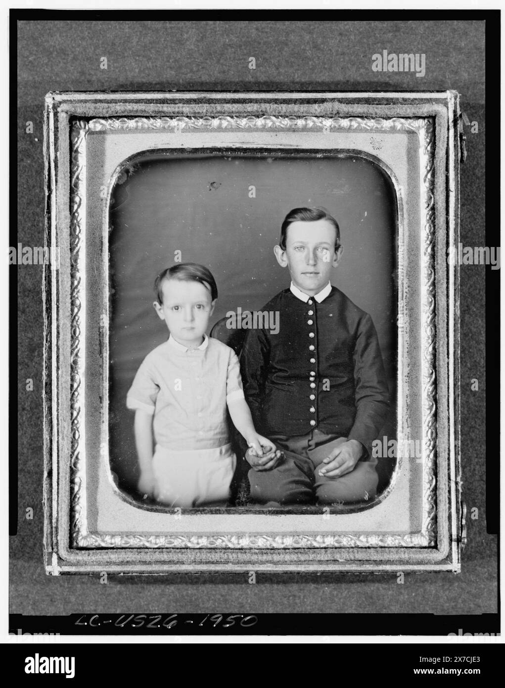 Unidentified boy seated in chair with child standing to left, three ...