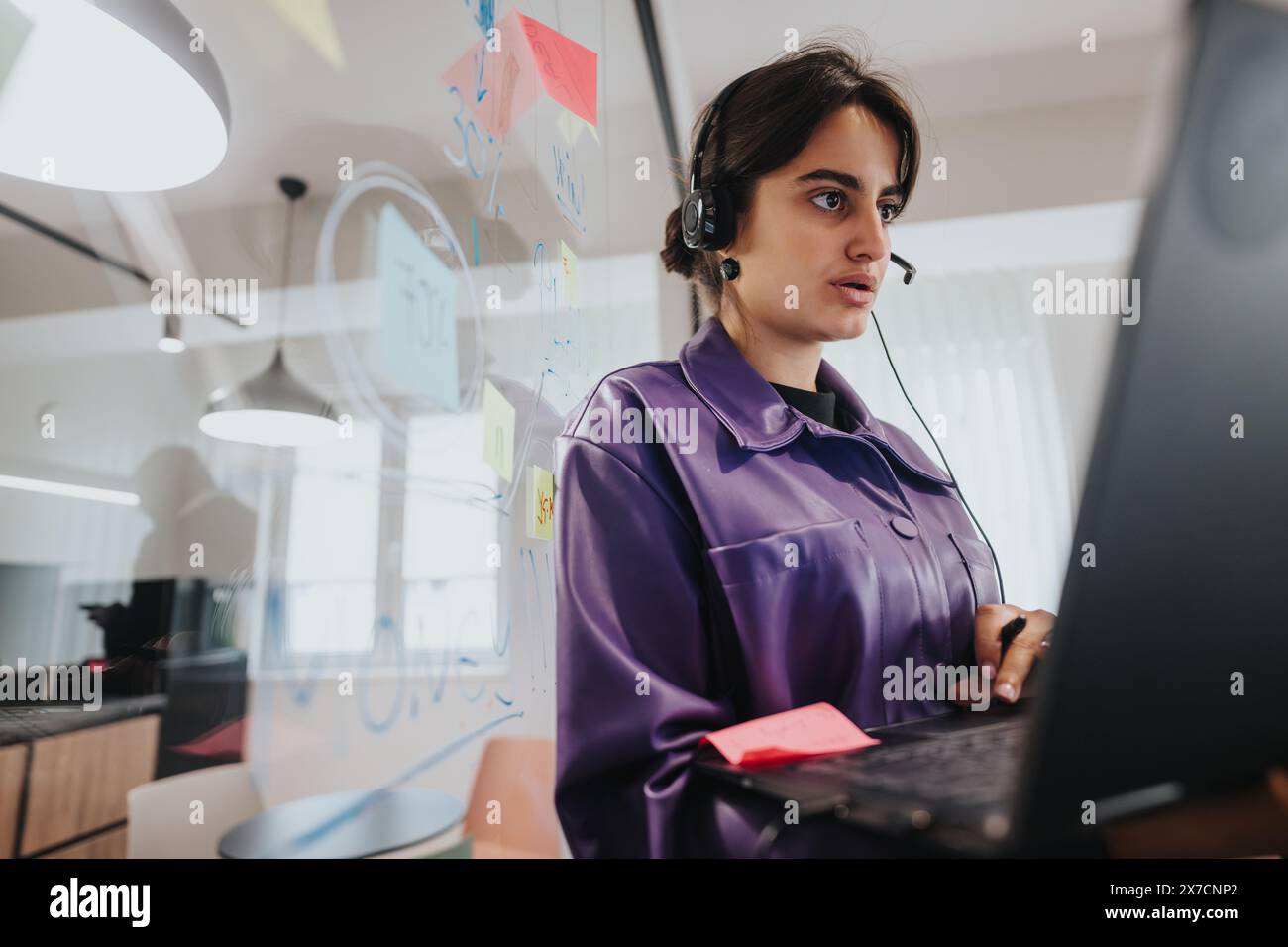 Focused female employee wearing headset during busy workday in modern ...