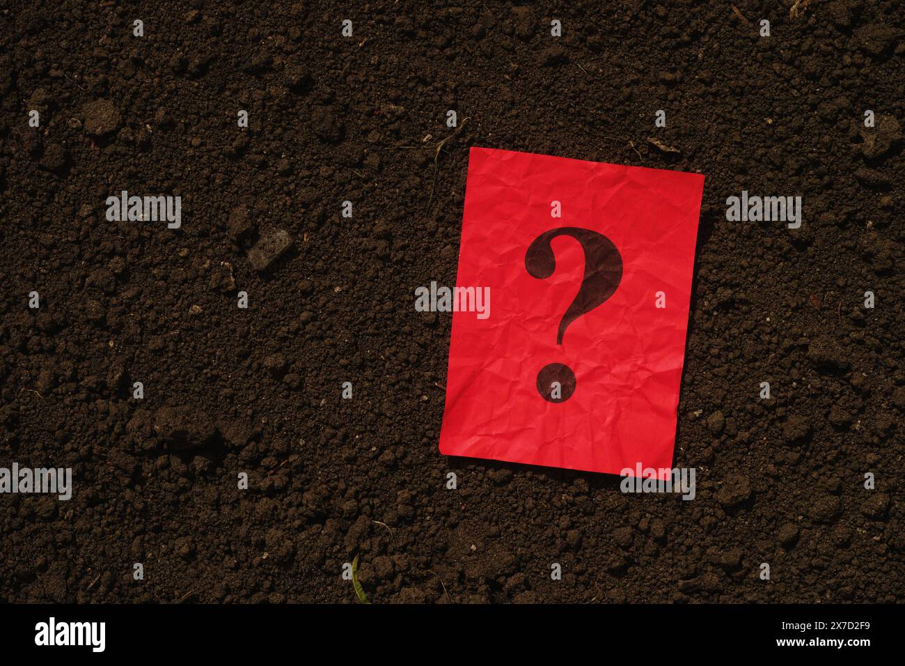 A red paper note with a question mark on it lying on a background of ...