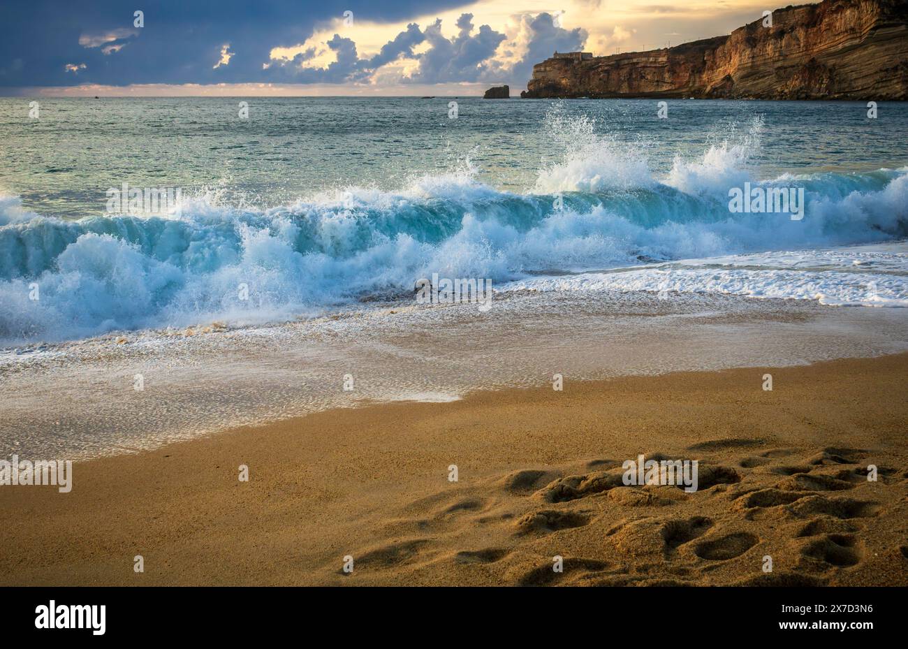 Footprints in the sand ahead of crashing waves at Nazare, Portugal ...