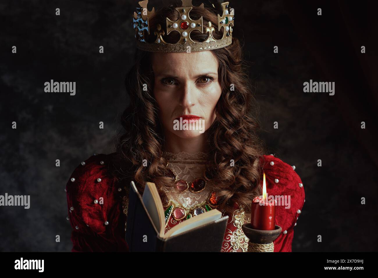 medieval queen in red dress with book, candle and crown on dark gray ...