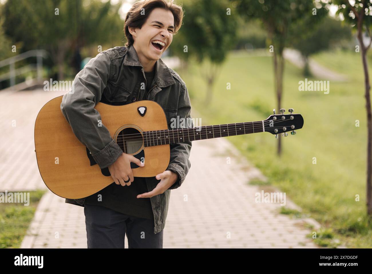 Smiled teenage boy musician playing acoustic guitar outdoor. Handsome ...