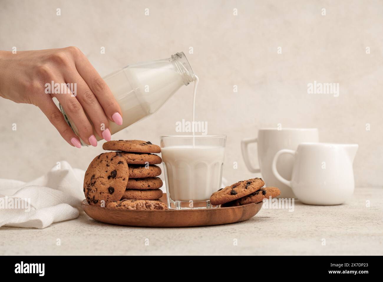 Woman pouring milk from bottle into glass and wooden plate of sweet ...