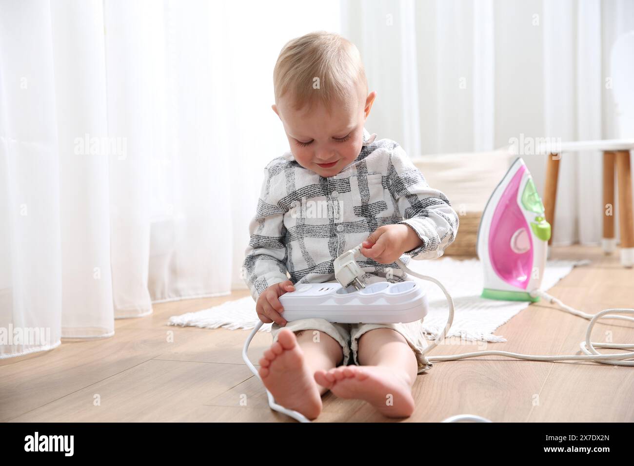 Little child playing with power strip and iron plug on floor at home ...