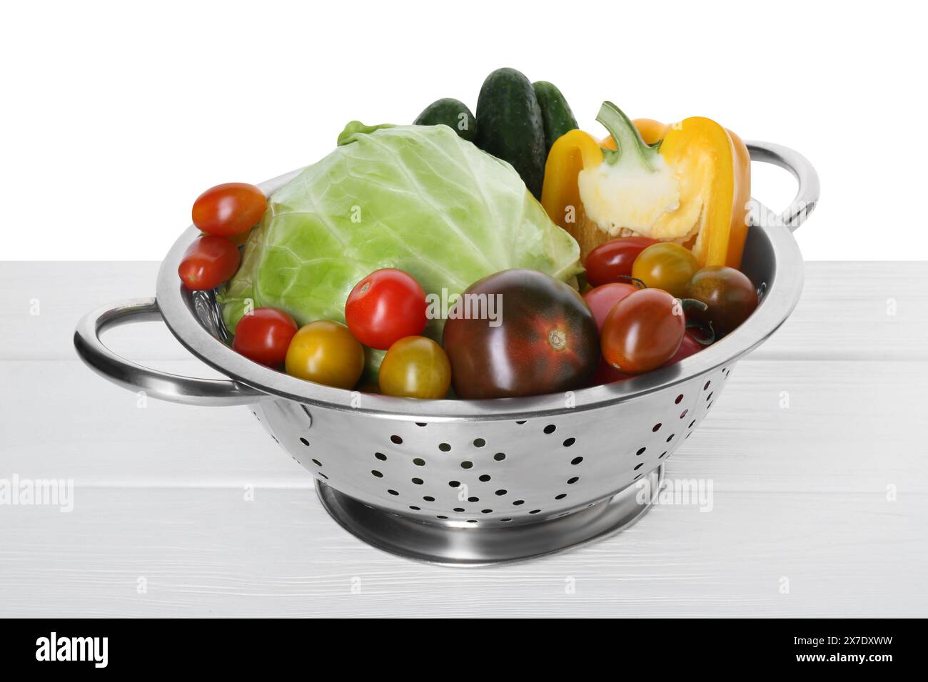 Metal colander with different vegetables on table against white ...