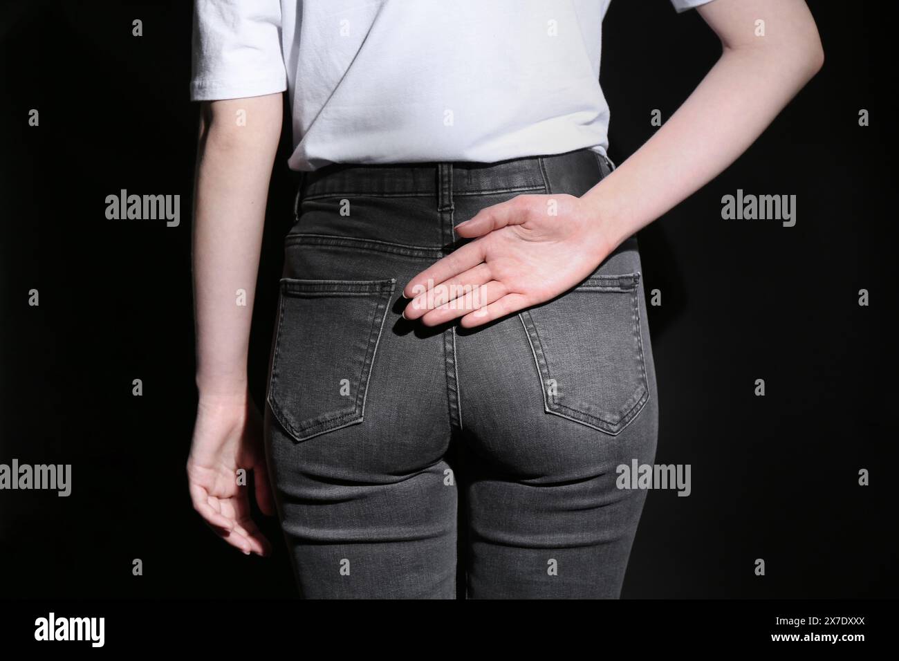 Woman showing open palm behind her back on black background, back view ...