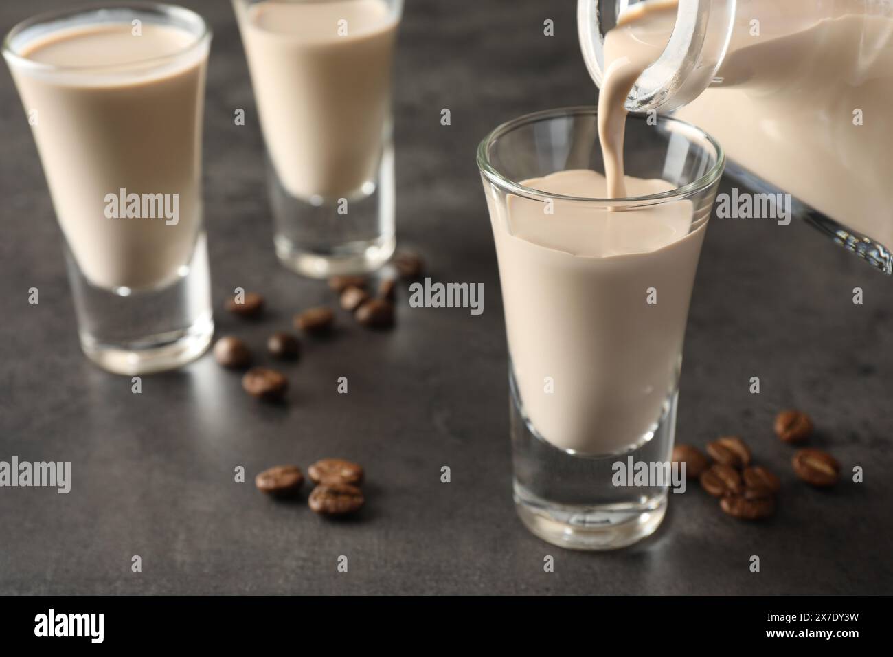 Pouring coffee cream liqueur into glass at grey table, closeup Stock ...