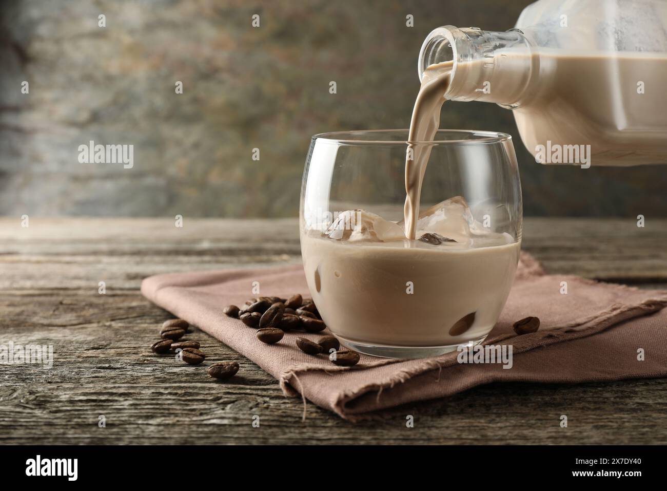 Pouring coffee cream liqueur into glass at wooden table, closeup Stock ...