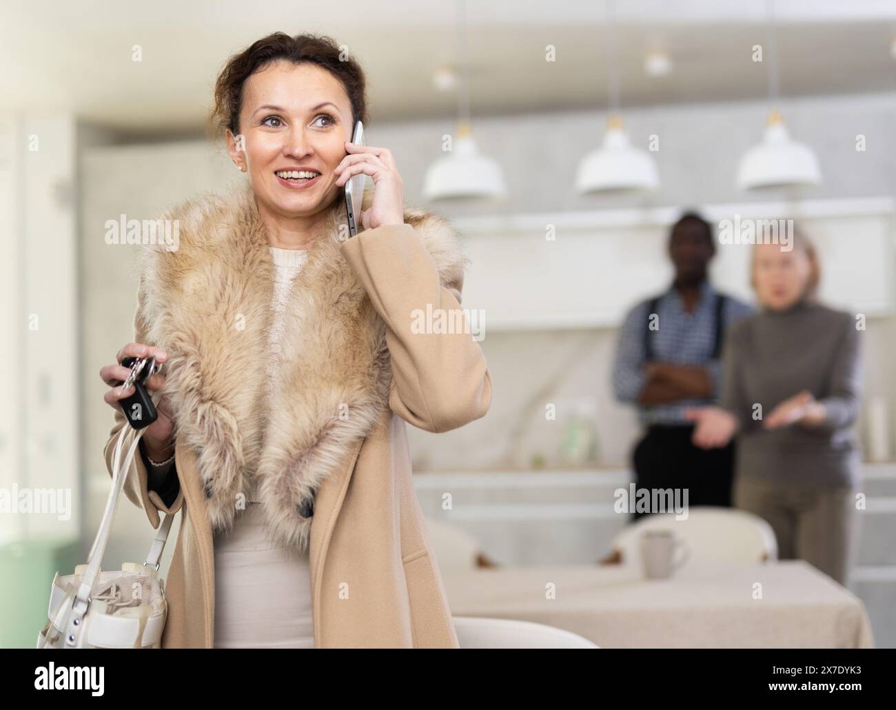 Middle-aged woman ready to leave talking on phone while male and female ...