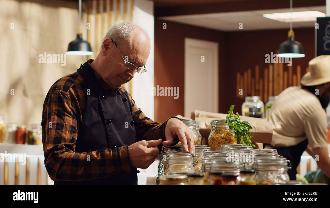 Portrait of smiling old zero waste vendor properly sealing bulk items ...