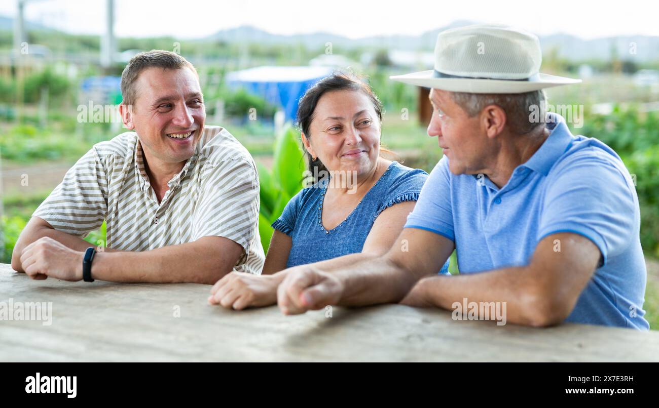 Happy farmers talking at village table Stock Photo - Alamy