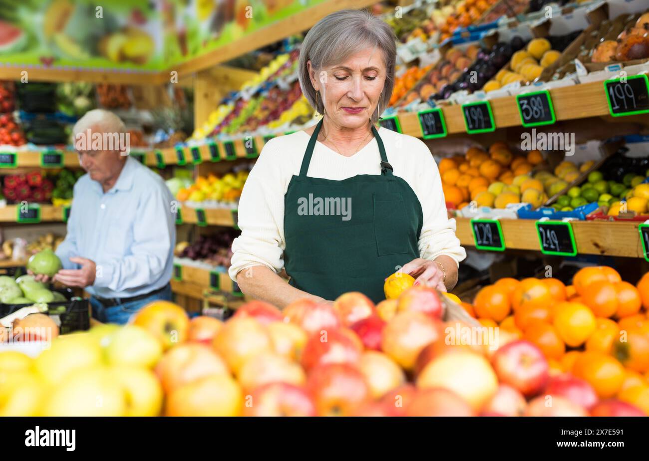 Woman merchandiser in apron putting goods on shelf in supermarket Stock ...
