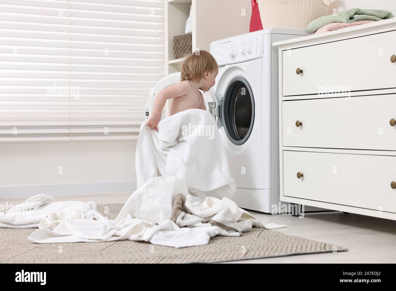 Little girl pulling baby clothes out of washing machine indoors Stock ...