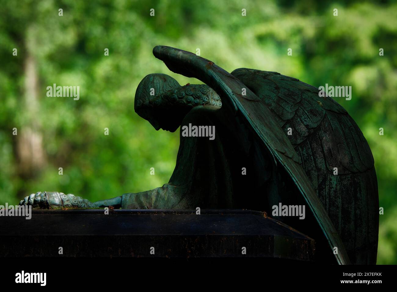 silhouette of an angel looking sadly downwards, bent over a gravestone ...