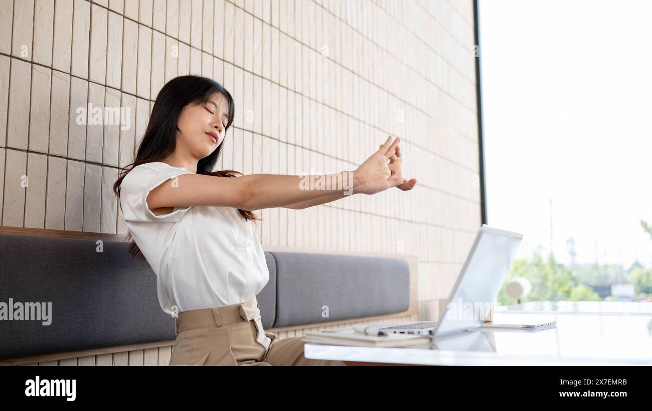 A beautiful Asian woman is feeling tired, stretching her hands and ...