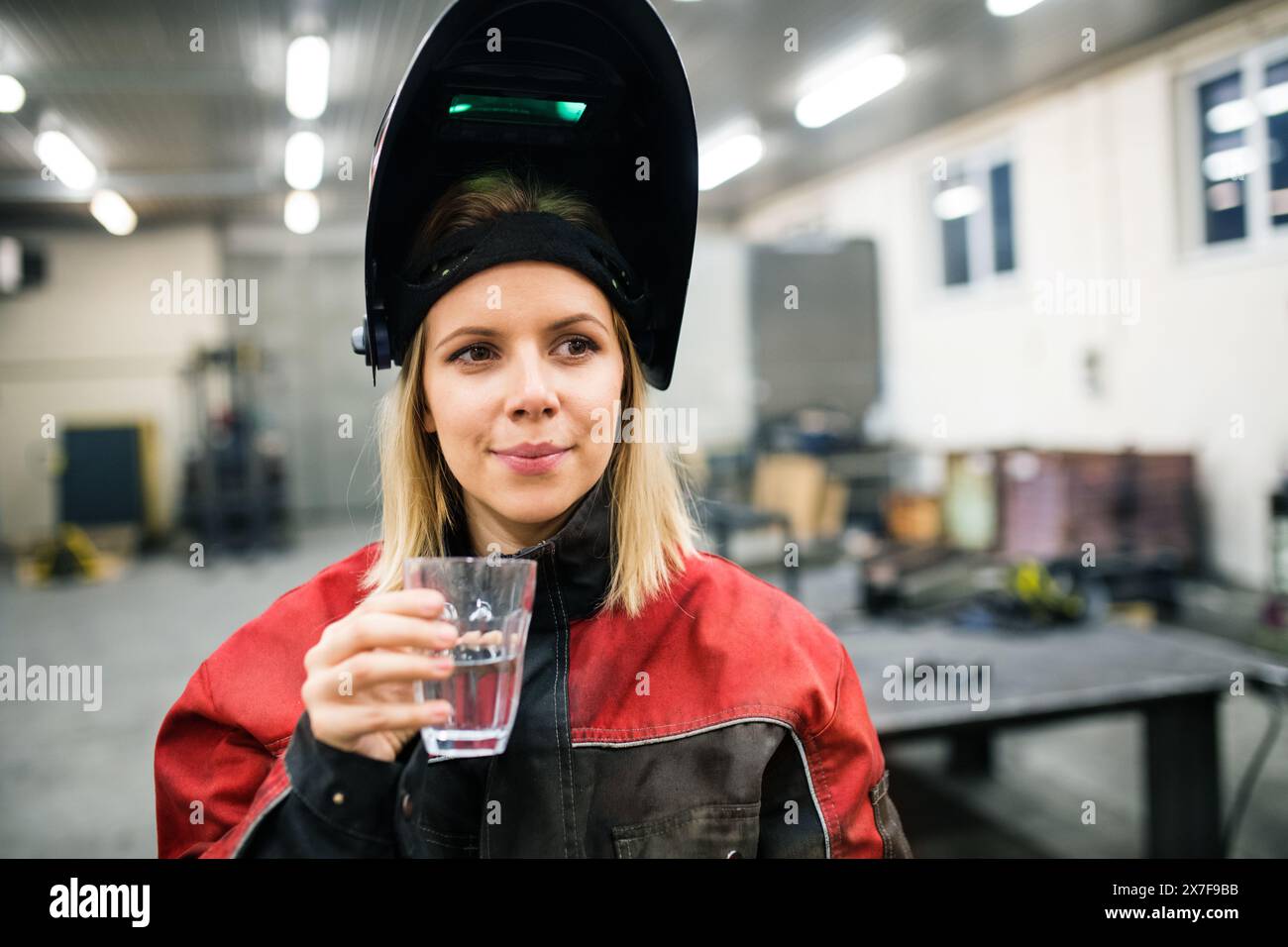 Beautiful blonde woman works as a welder in workshop, drinking water ...
