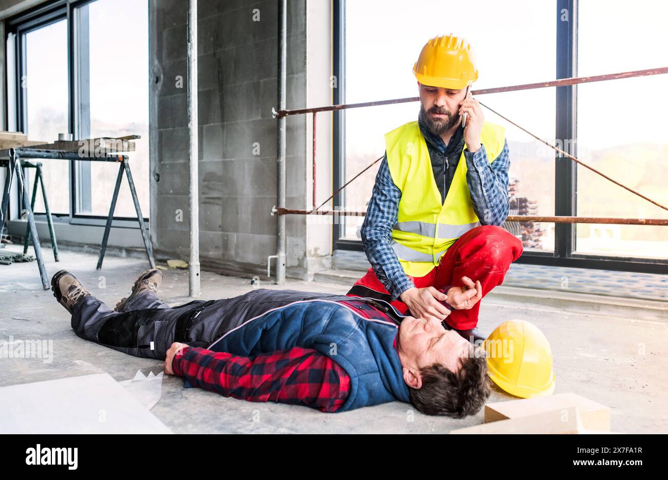 Colleague giving first aid to unconscious worker after accident ...