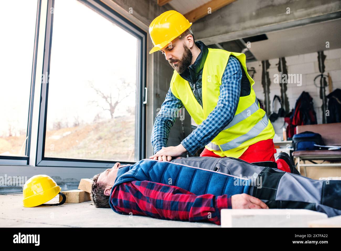 Colleague performing CPR on an injured worker lying on the ground after ...