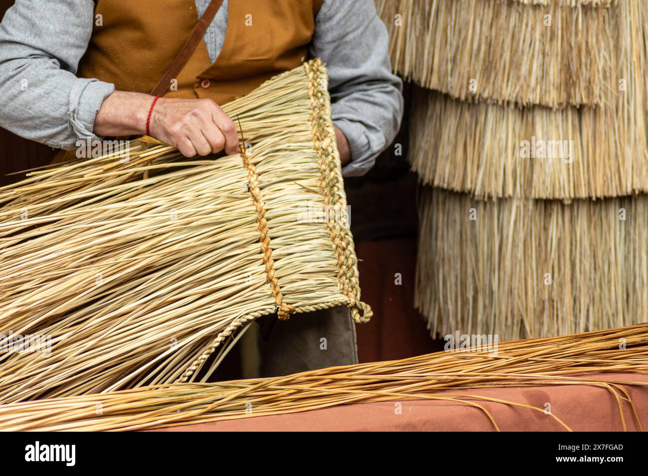 hands of an artisan weaving a traditional waterproof cape with straw ...
