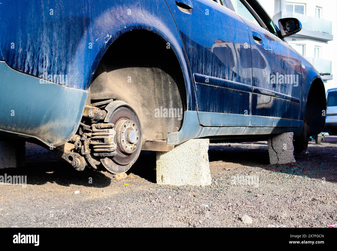 A blue car with a tire resting on top of a block in an abandoned ...