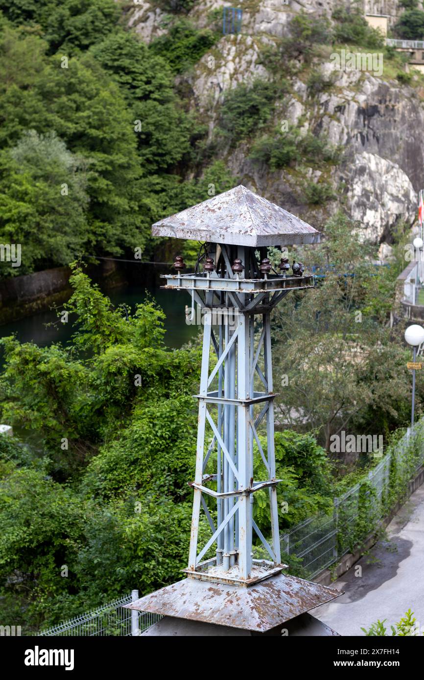 A tall, rusted industrial tower stands amidst lush greenery and rocky terrain, highlighting the ...