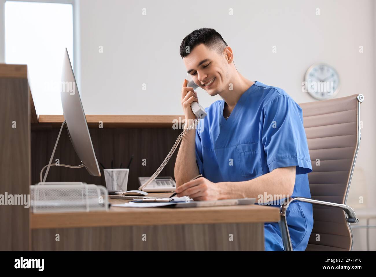 Smiling medical assistant talking by phone at hospital reception Stock ...