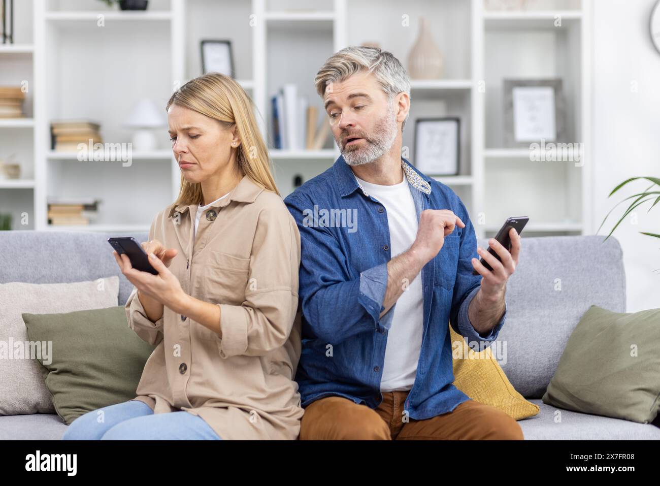 Couple sitting on couch looking upset while using smartphones ...
