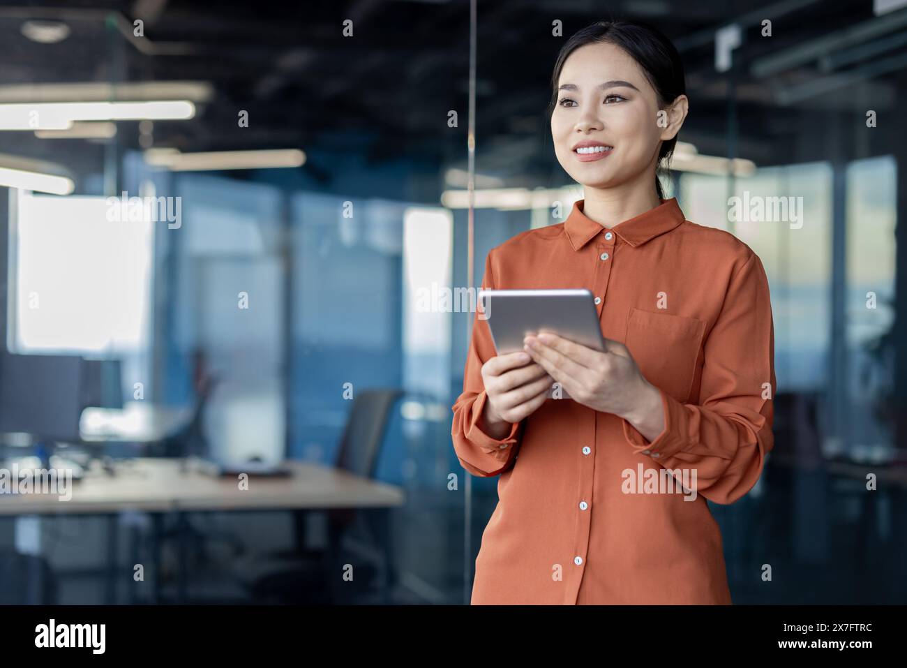 Confident Asian businesswoman using digital tablet in modern office, looking inspired and ready ...