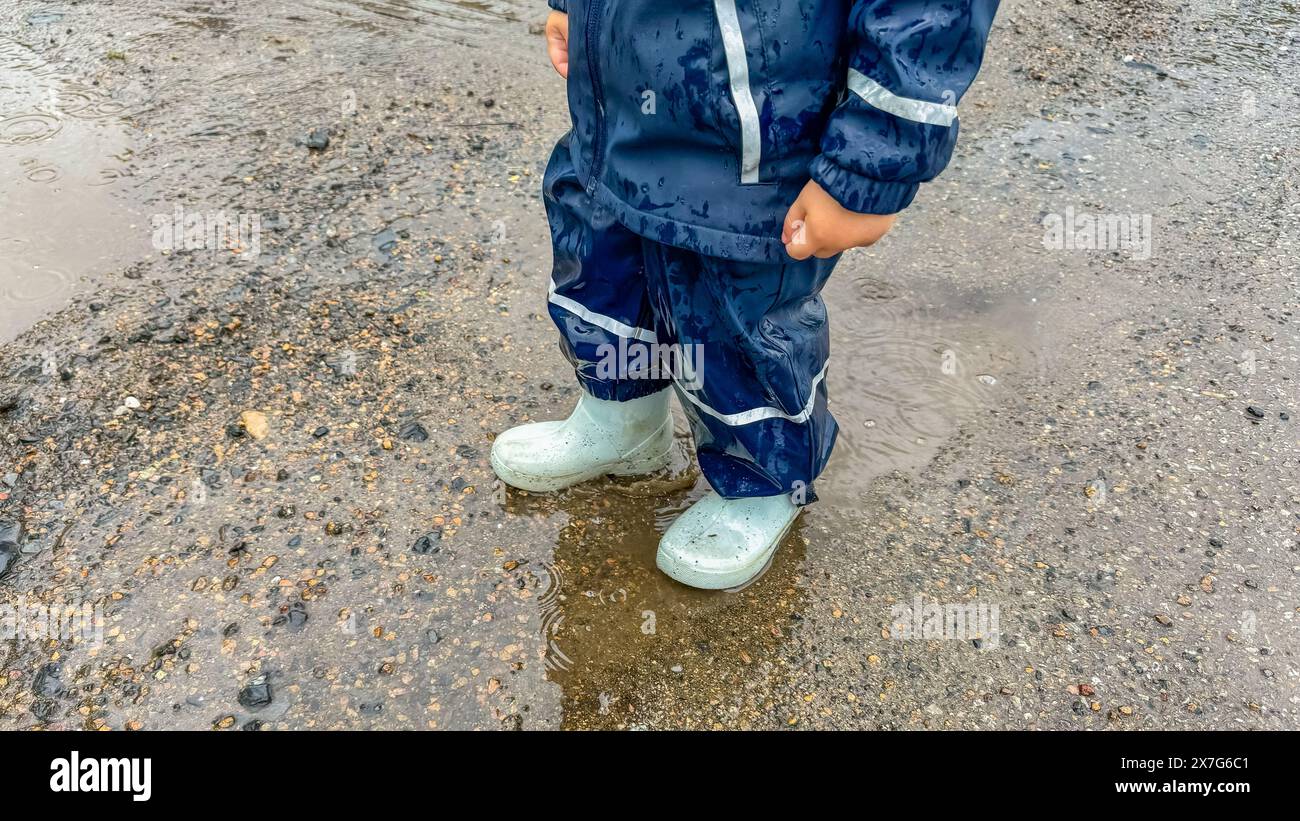 The child runs through puddles in rubber boots and a waterproof suit ...