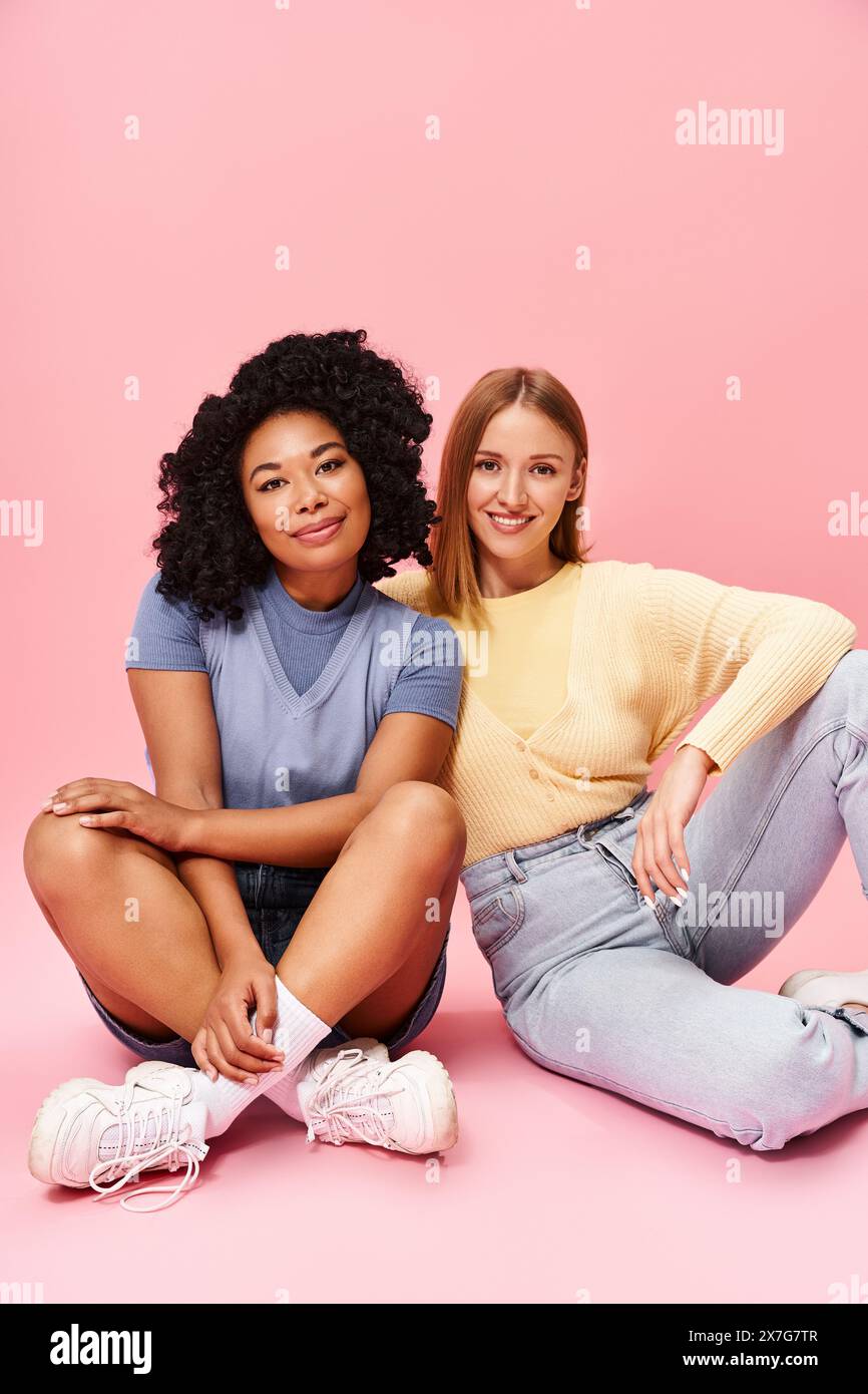 Two diverse women in cozy outfits sit on the ground, striking a pose ...