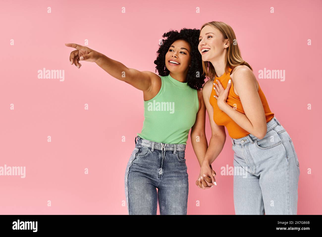 Two attractive diverse women pointing at something, standing next to ...