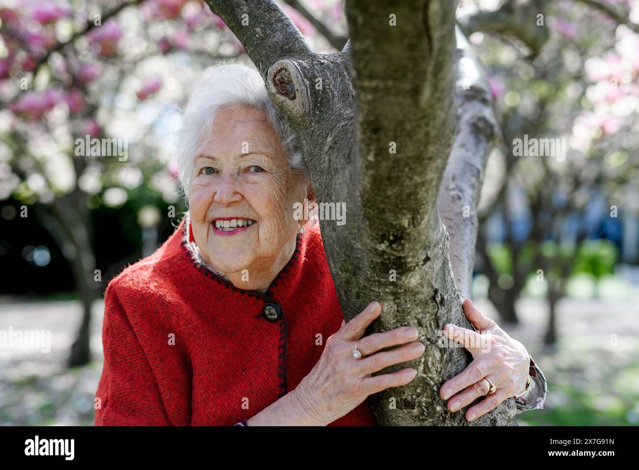 Portrait of elderly woman standing by magnolia tree, in park, having ...