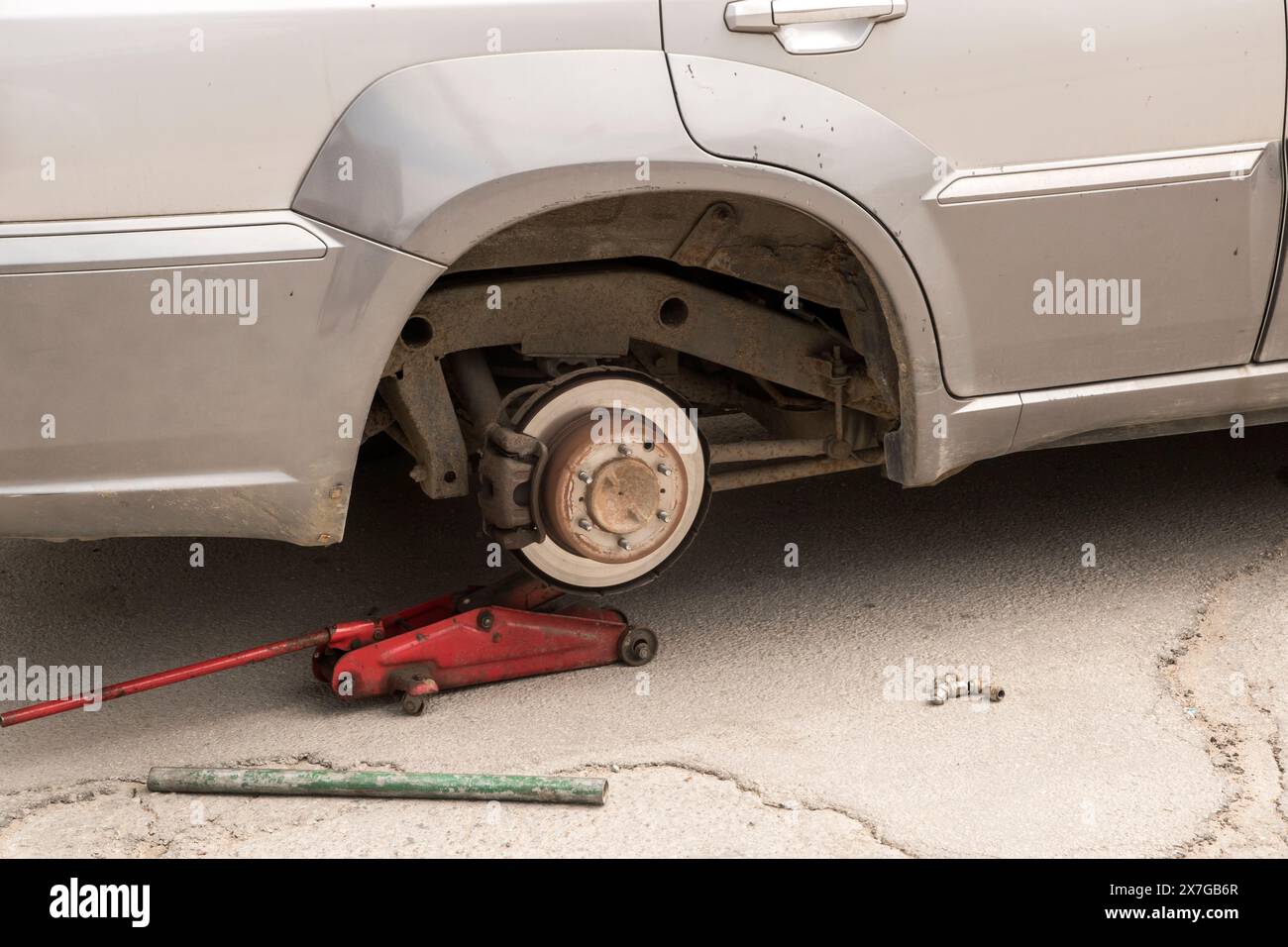 Car on jack lift with one tire removed reveal the rusty disc brake ...