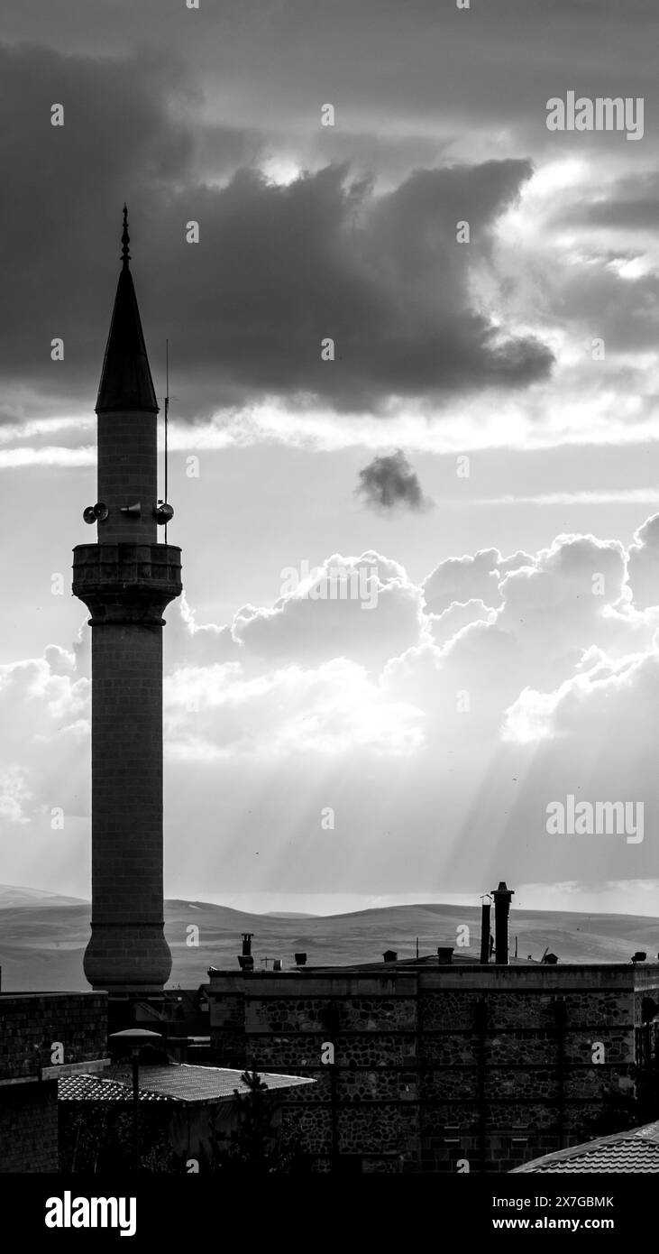 Minaret silhouette with sun rays through clouds in black and white ...