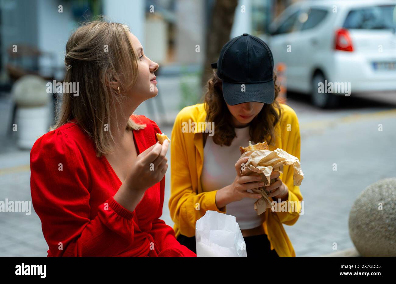 Two girls eat street food on a bench Stock Photo - Alamy