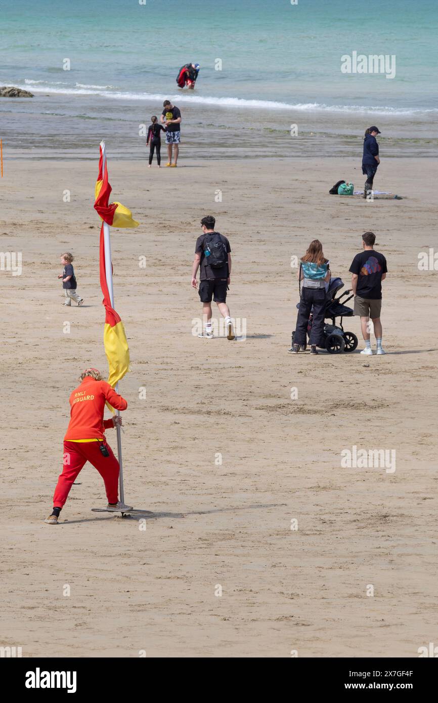A RNLI Lifeguard setting up a yellow and red safety flag on Towan beach ...