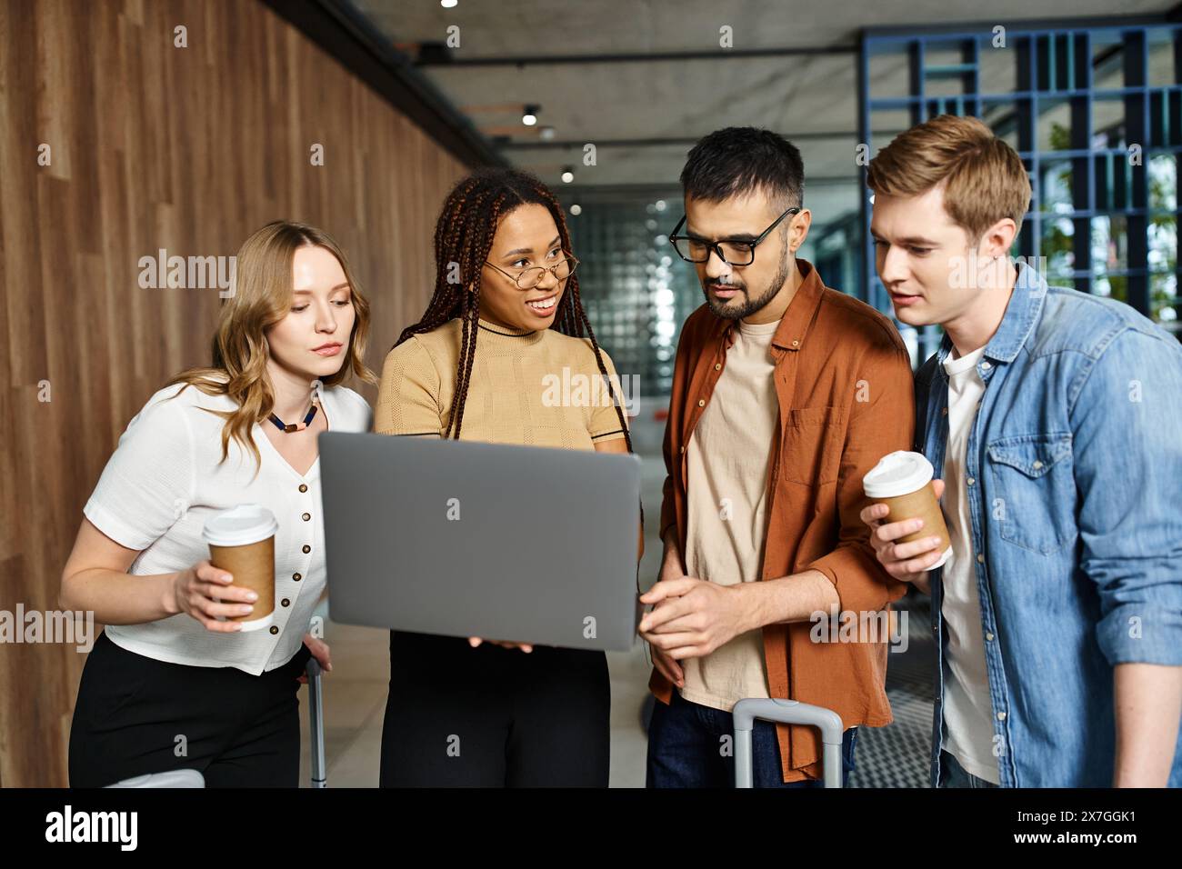 Multicultural colleagues in casual attire gather around a laptop for a ...
