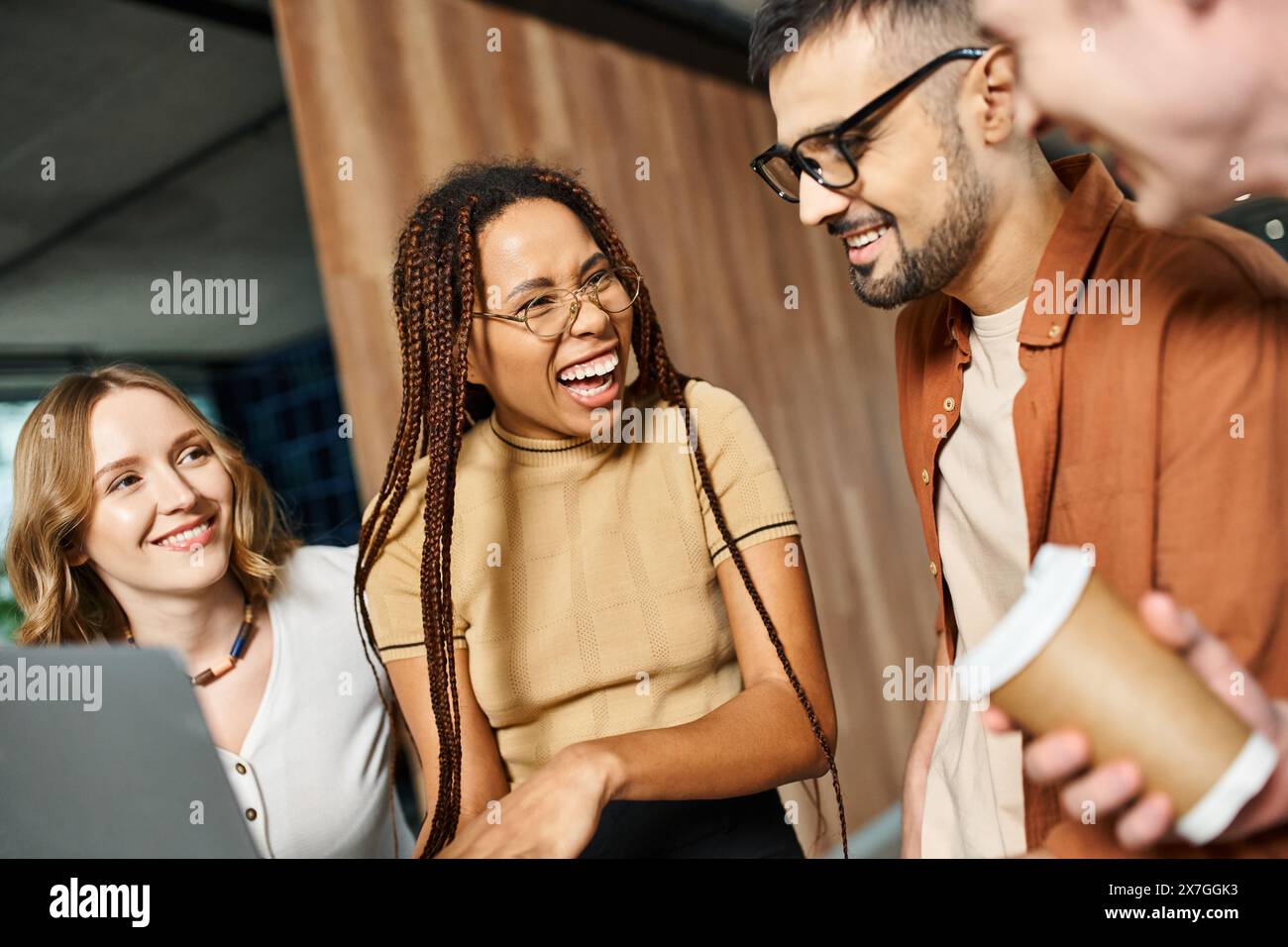 Multicultural colleagues in casual attire gather around a laptop in a ...
