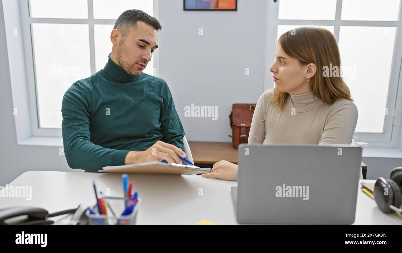 A man and woman coworking in a bright modern office discuss over a ...