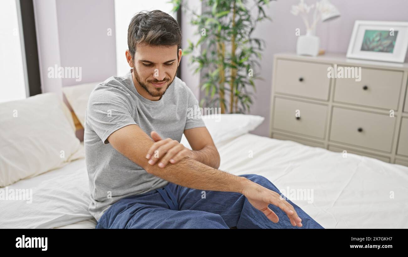 Hispanic man applying lotion to elbow in a bedroom setting, depicting ...