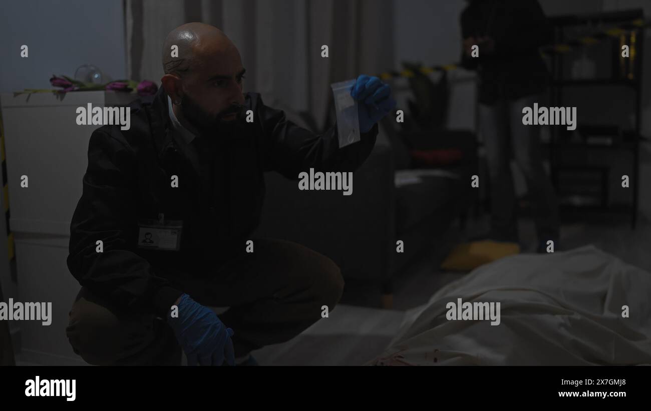 A bald man examines evidence at an indoor crime scene with a covered ...