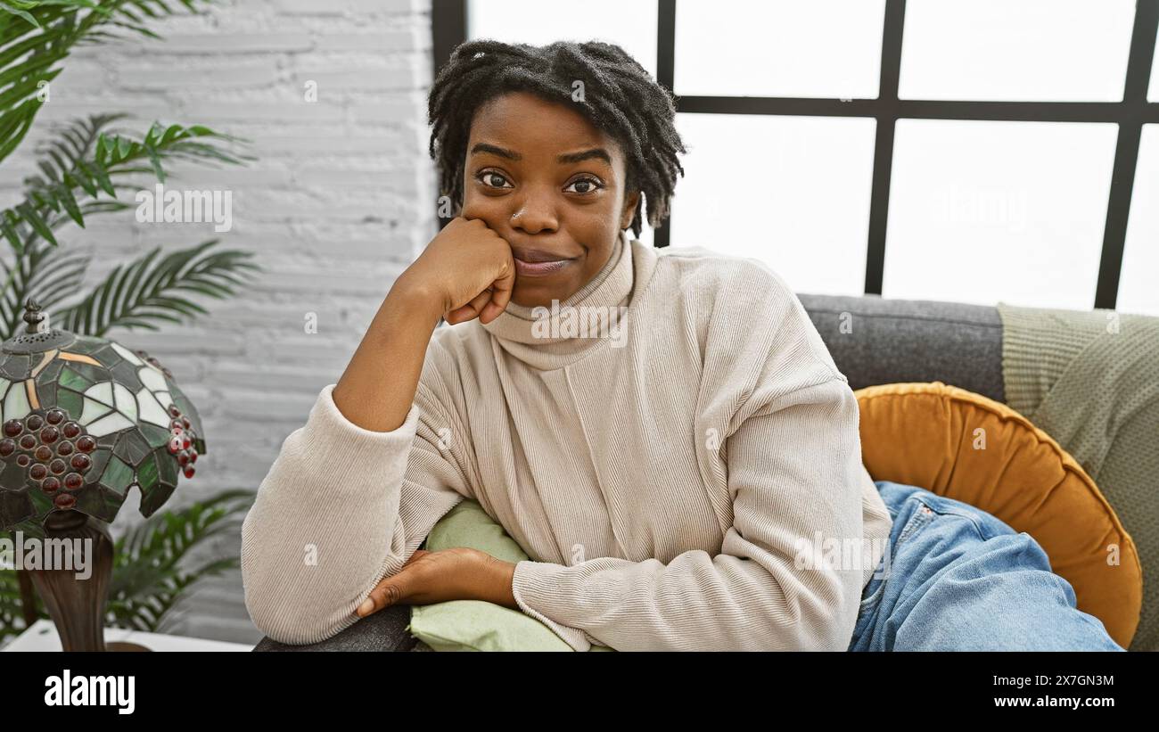 Smiling young black woman with dreadlocks seated casually in a cozy ...