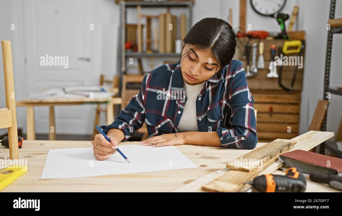 A young indian woman concentrates while drafting in a woodwork workshop ...