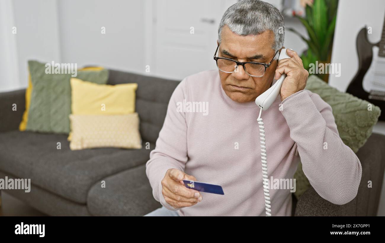 Mature man with glasses holding a credit card and talking on a landline ...