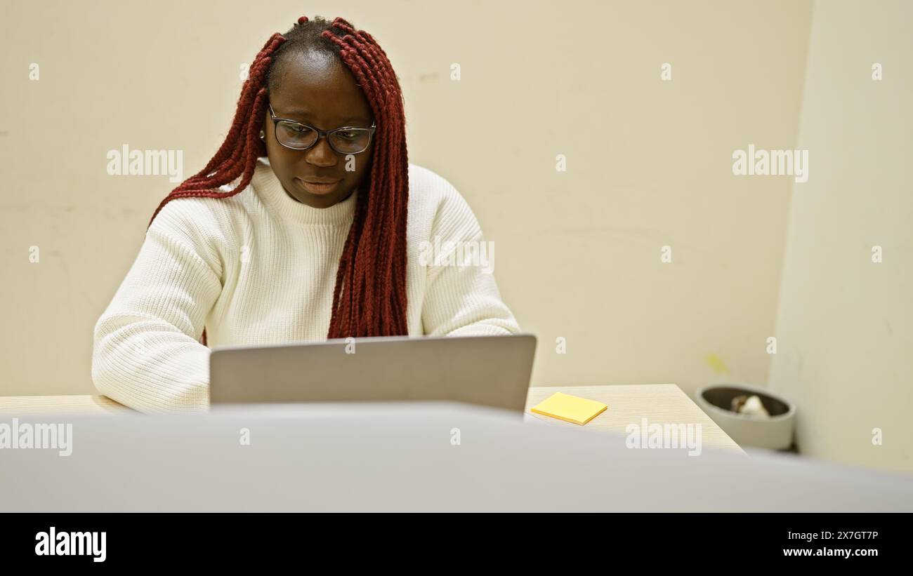 Focused african woman with braids working in an office using a laptop ...