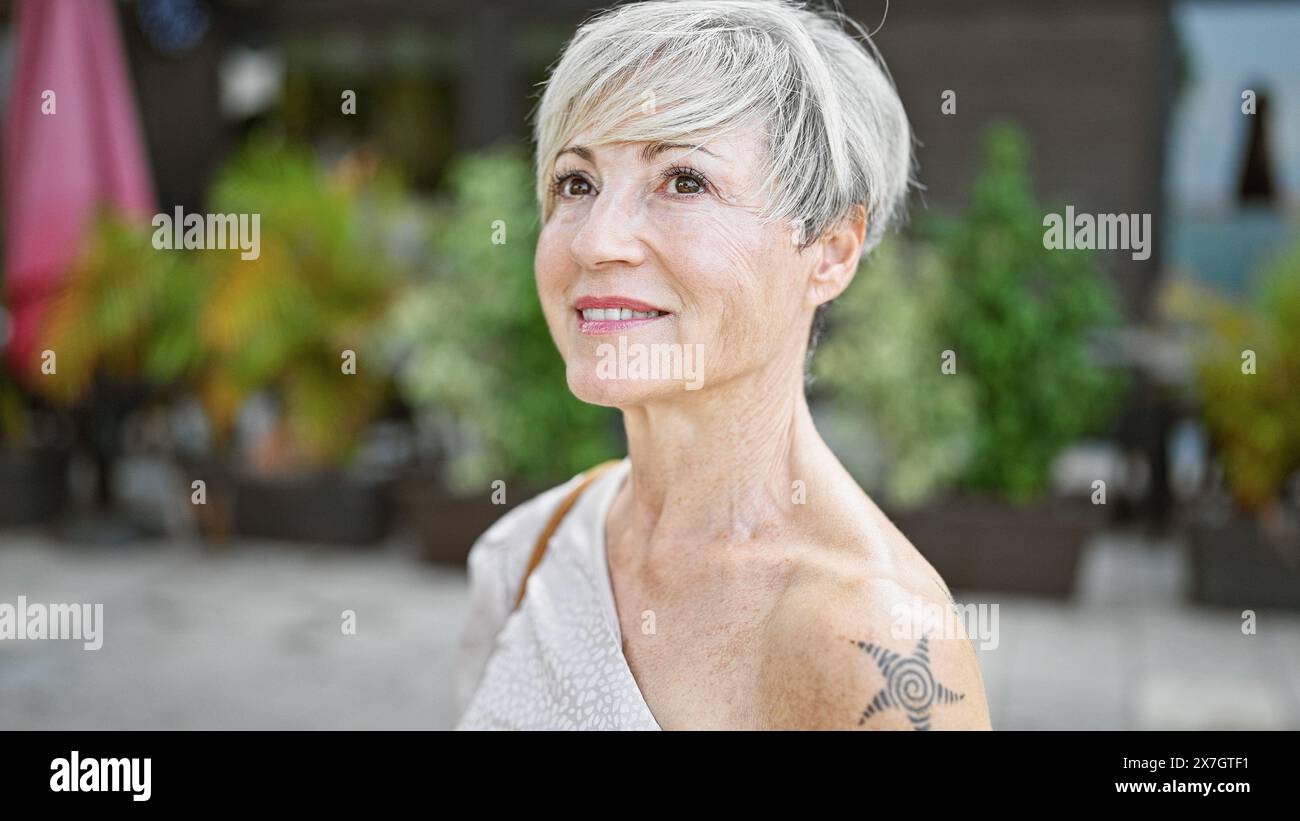 A mature woman with short grey hair smiles gently in an outdoor urban ...