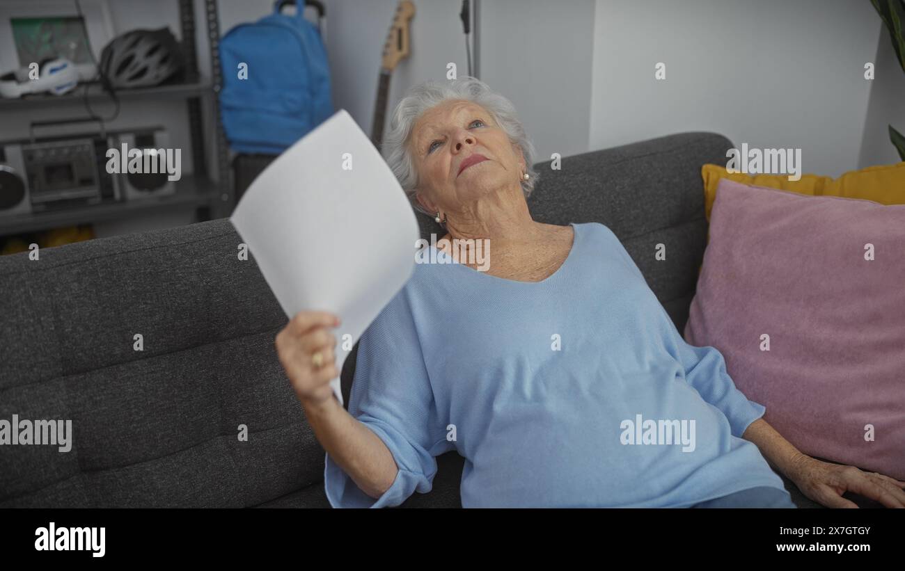 Elderly woman fanning herself with paper in a cozy living room Stock ...
