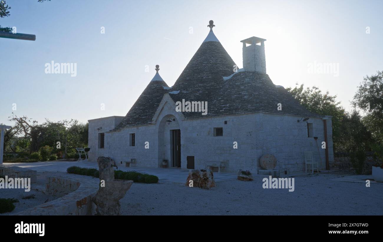 A traditional trullo house with stone walls and conical roofs is bathed ...
