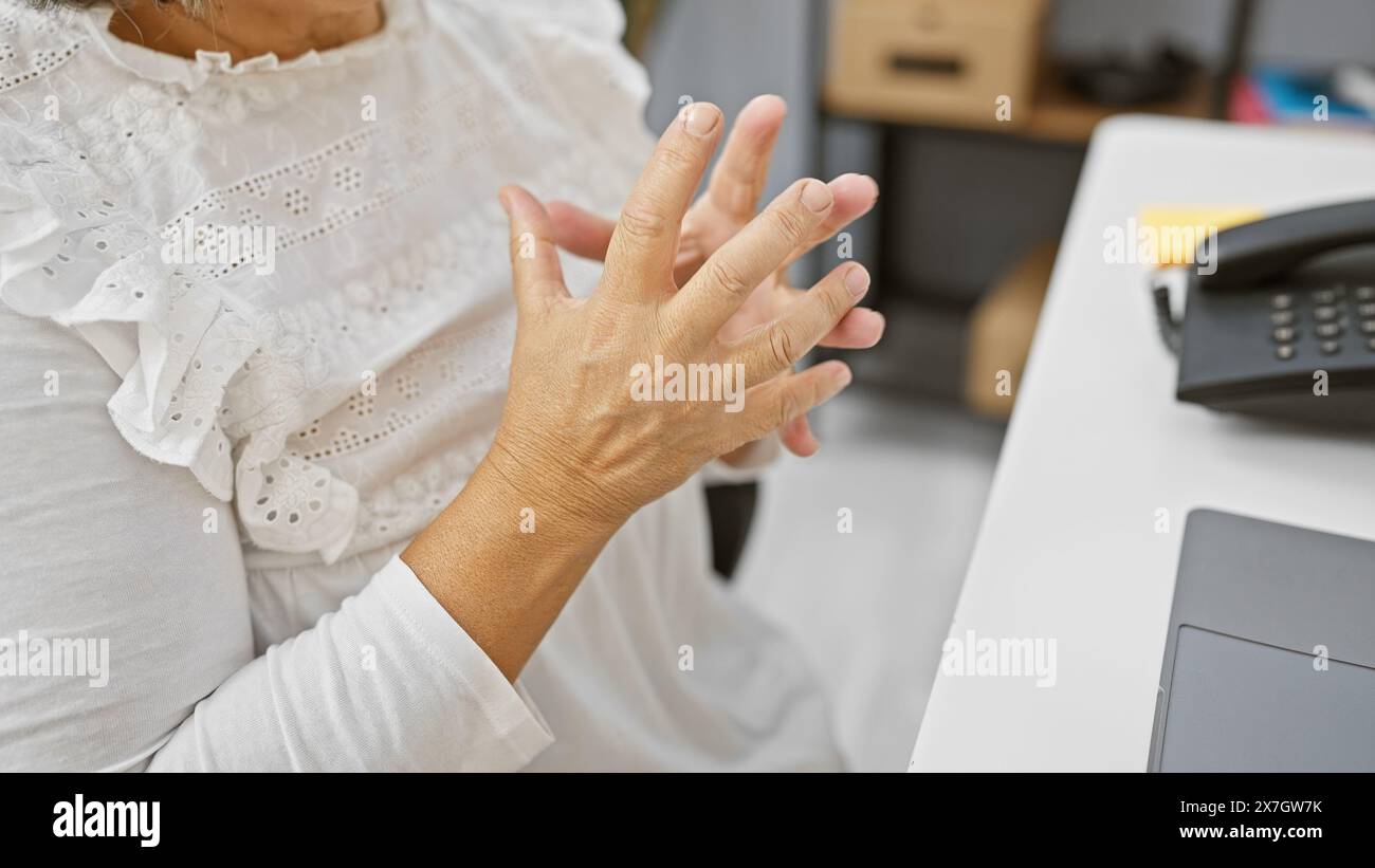 Mature woman experiencing hand pain at her office desk, perhaps from ...